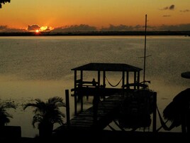 Um cais se estendendo sobre águas calmas, com um pôr do sol ao fundo.