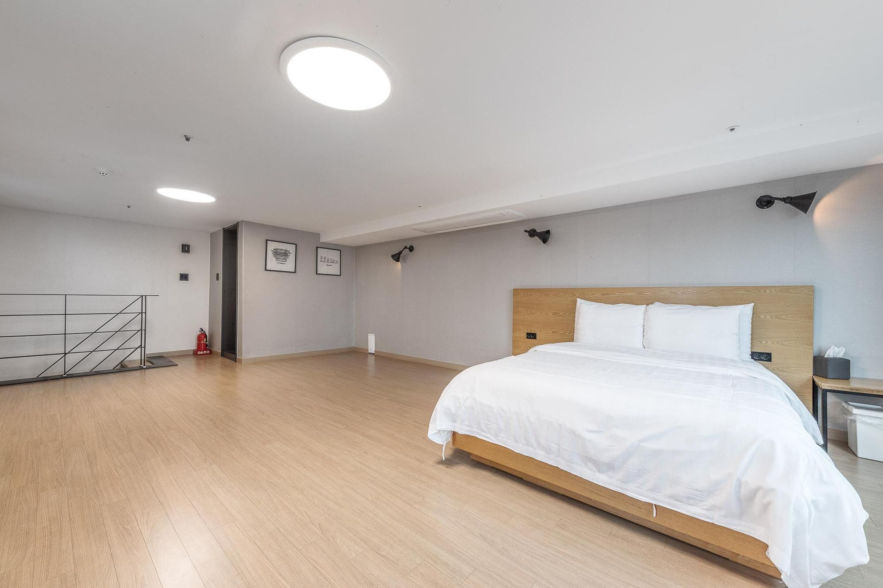 Quarto de hotel com uma cama grande, cabeceira de madeira, mesa de cabeceira e uma pequena mesa com luminária.