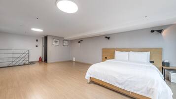 Quarto de hotel com uma cama grande, cabeceira de madeira, mesa de cabeceira e uma pequena mesa com luminária.