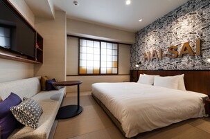 Quarto de hotel com cama, sofá, televisão, mesinha e parede com caracteres japoneses.