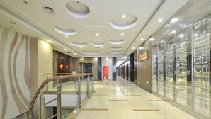 Um corredor com corrimão de vidro, piso de azulejo e luminárias circulares no teto.