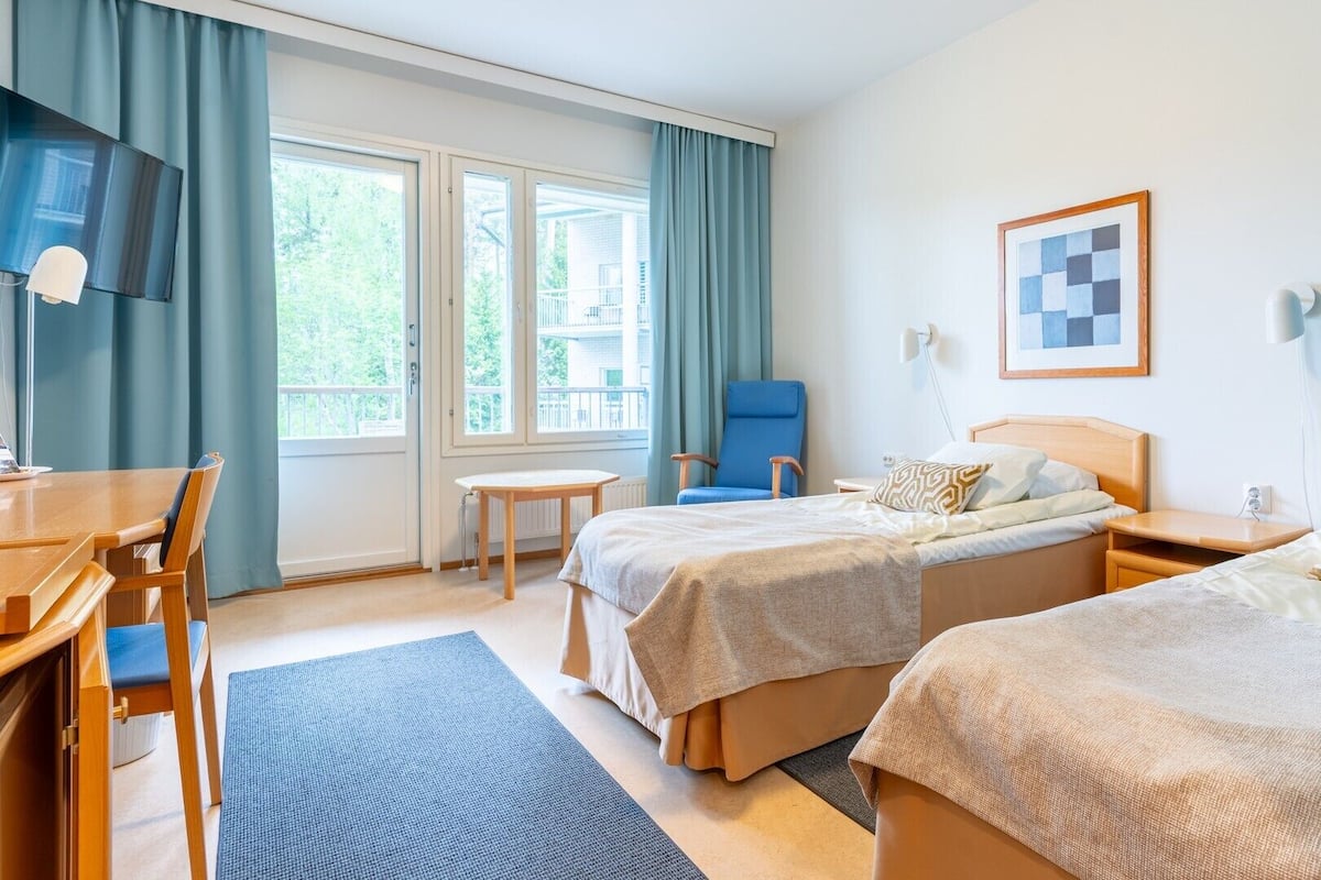 Quarto de hotel com duas camas, uma escrivaninha, uma cadeira e uma televisão.