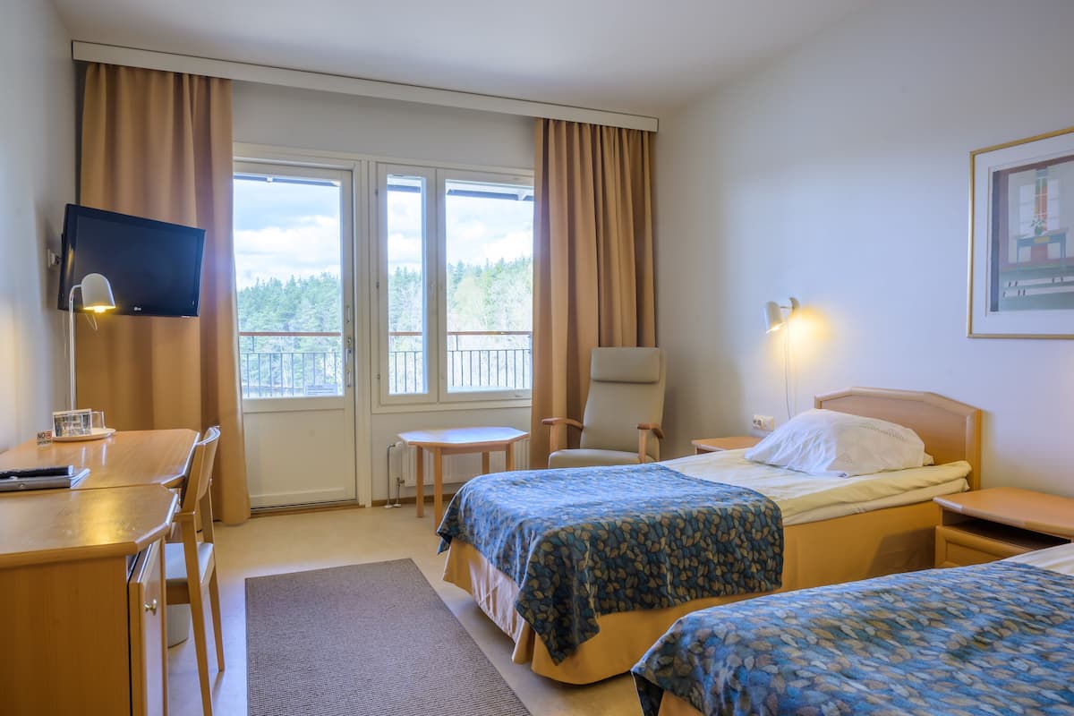Quarto de hotel com duas camas, uma escrivaninha, uma cadeira, televisão e vista para a varanda.