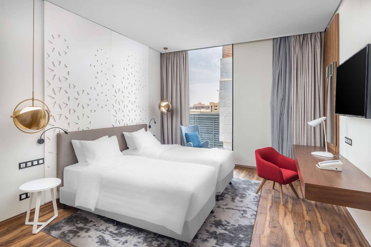 Quarto de hotel com cama, escrivaninha, cadeira, televisão e vista para a cidade.