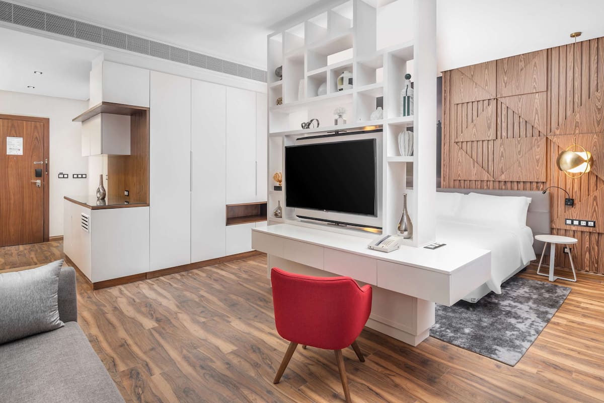 Quarto moderno com uma cama grande, escrivaninha com televisão e prateleiras embutidas.