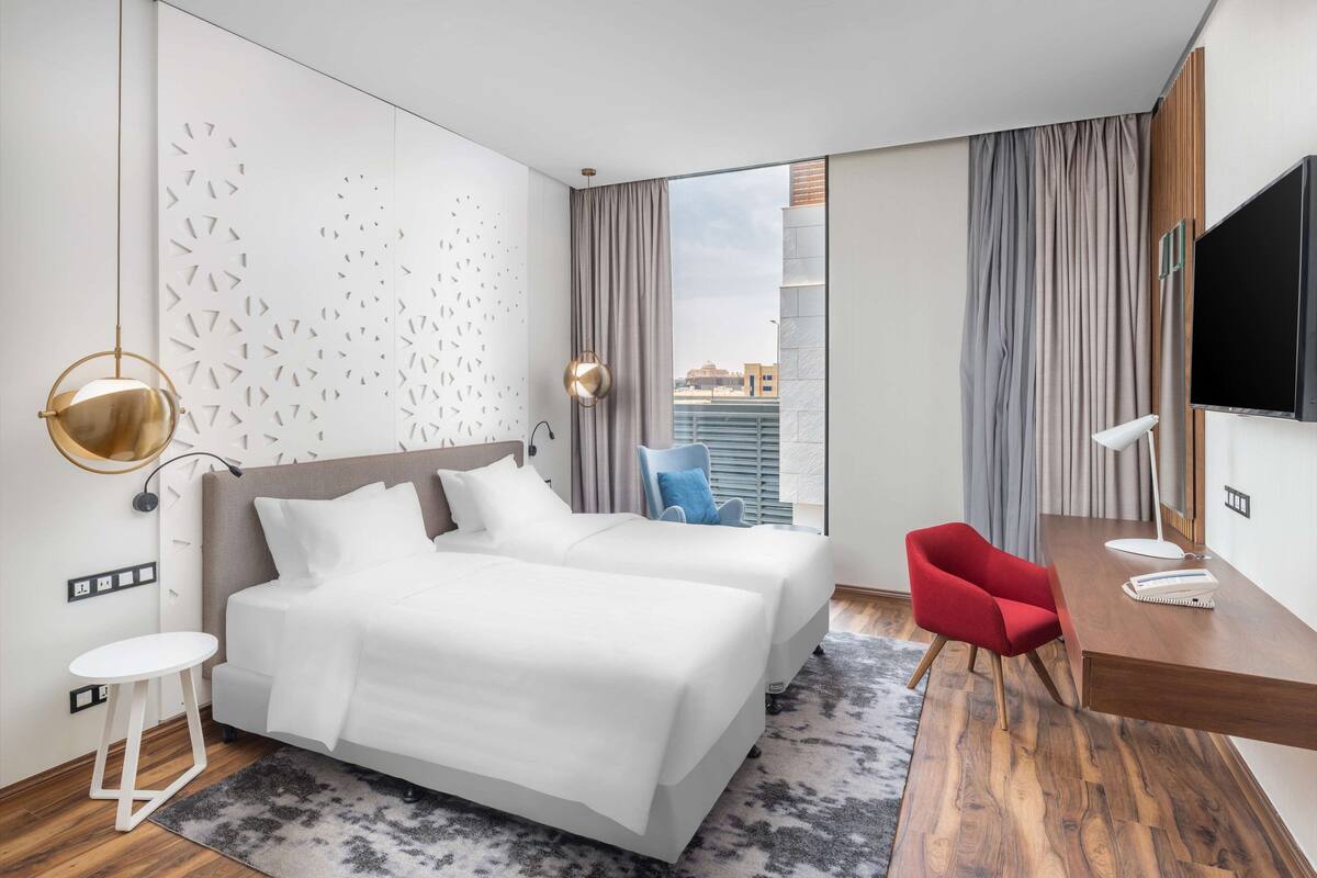 Quarto de hotel moderno com uma cama grande, uma escrivaninha, uma televisão e vista para a cidade.
