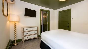 Quarto com cama, cômoda, luminária, televisão e porta.