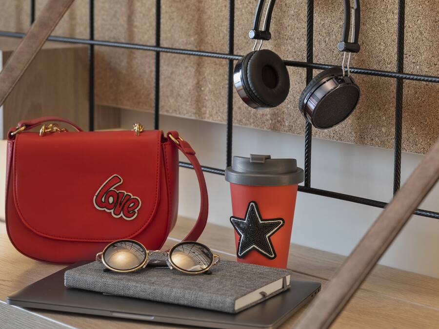 Uma bolsa vermelha com bordado a dizer 'Love', uma chávena com tema de estrelas e um par de óculos sobre uma mesa.