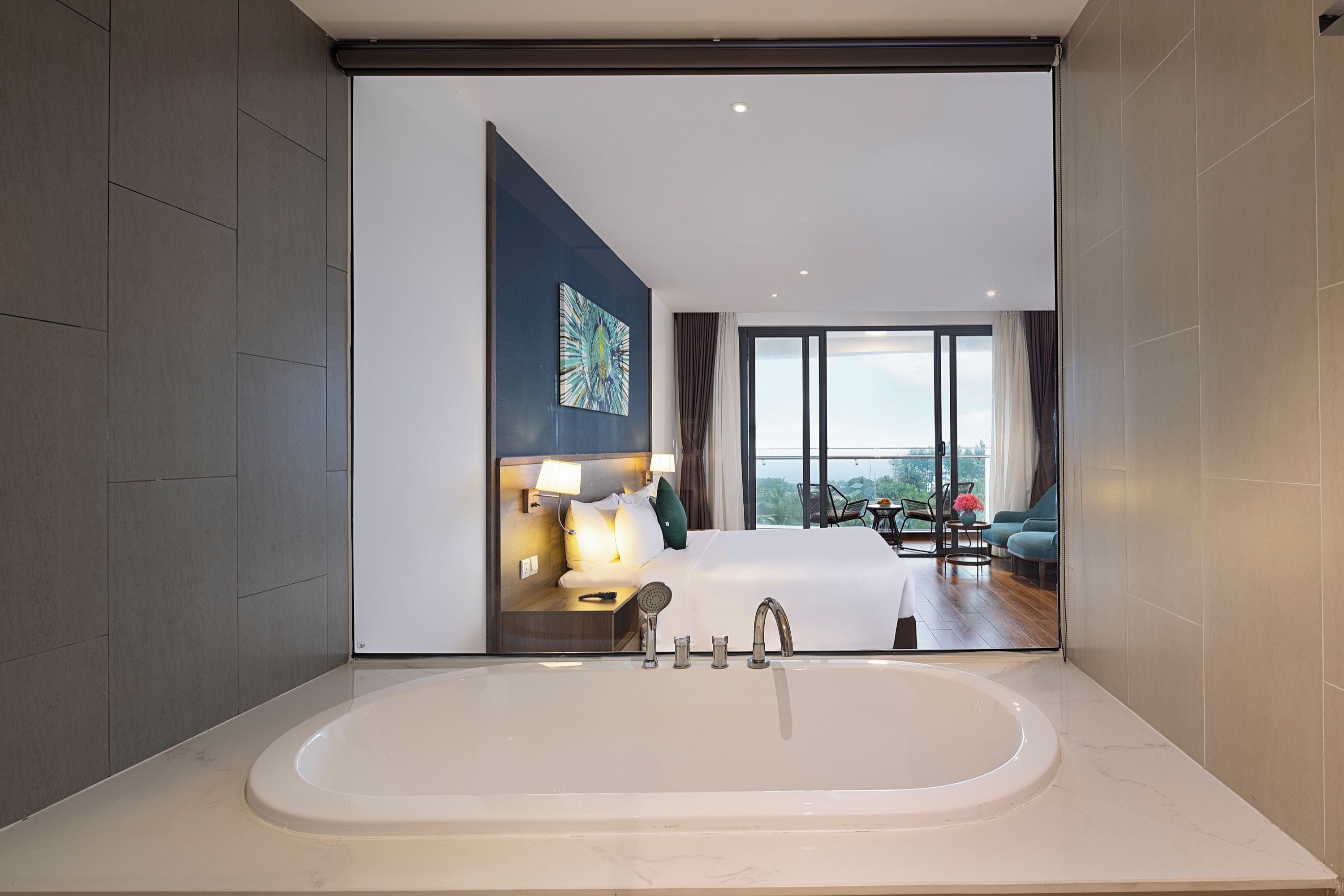 Casa de banho de hotel moderna com uma banheira grande, área de chuveiro separada e vista para o quarto com varanda.
