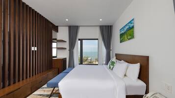 Quarto de hotel moderno com uma cama grande, painéis de madeira, vista para o mar e uma pintura na parede.