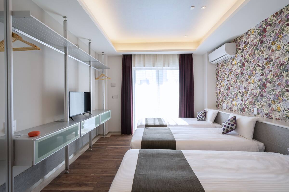 Quarto de hotel moderno com duas camas, televisão, escrivaninha e guarda-roupa.
