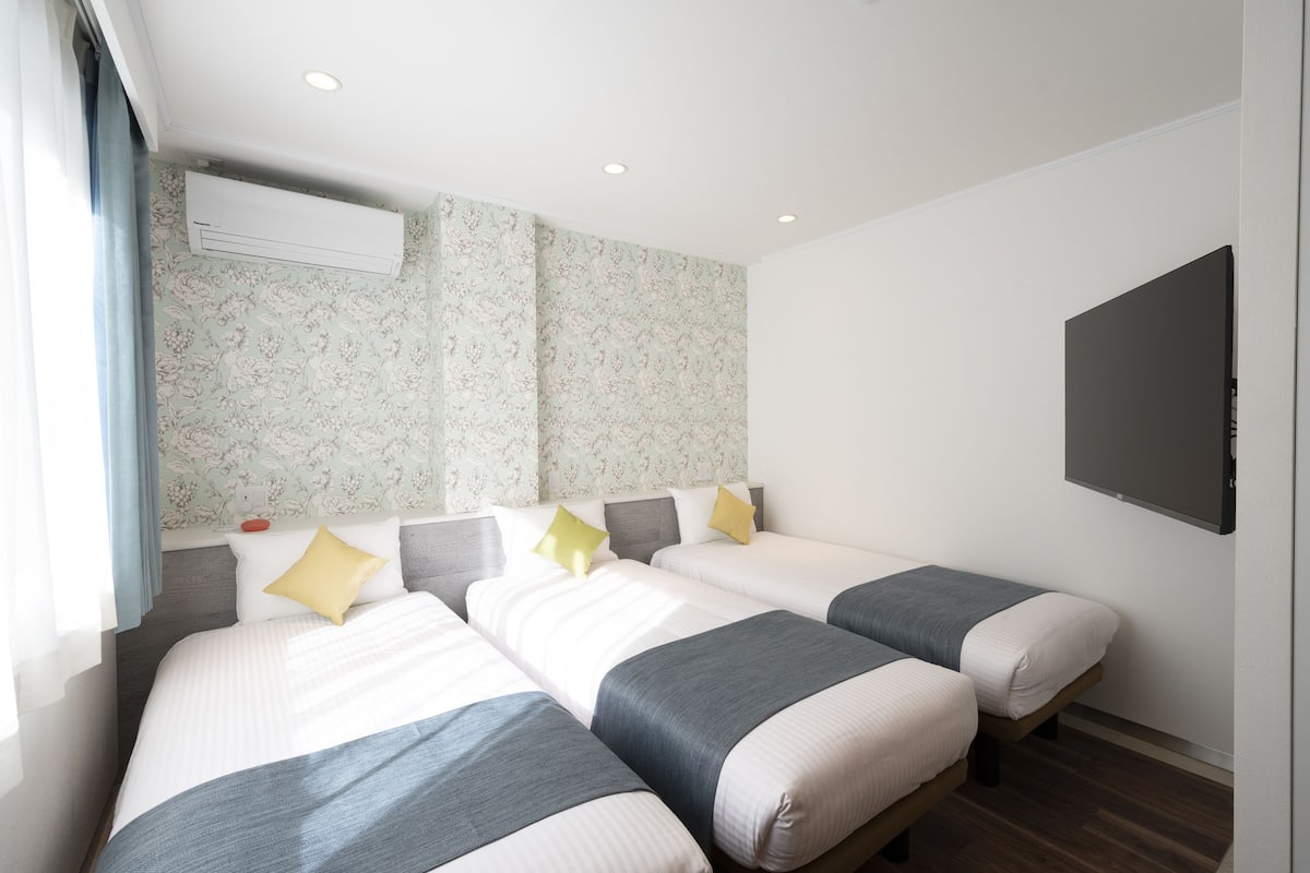 Quarto de hotel com três camas, televisão de tela plana e ar condicionado.