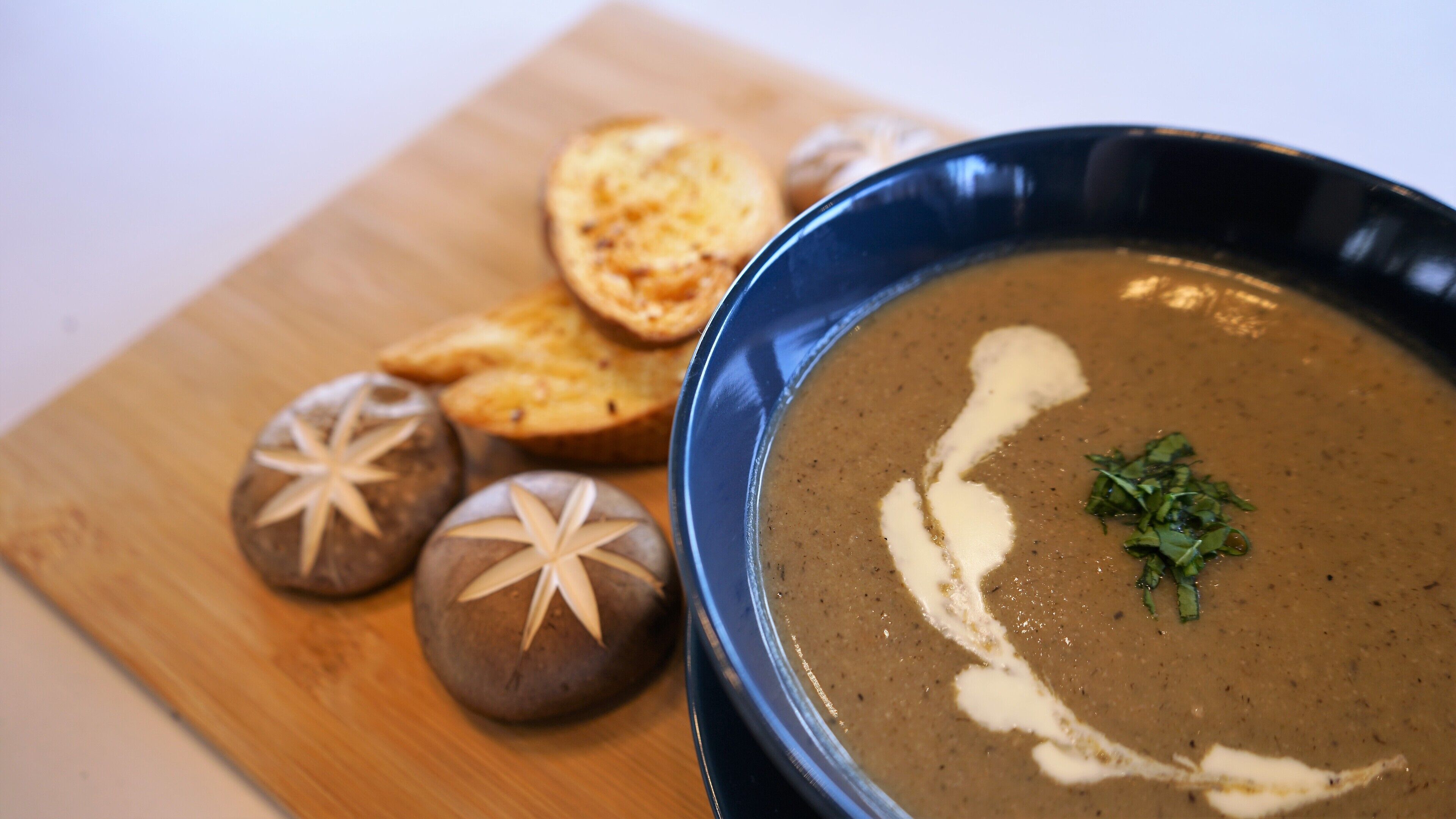 Uma tigela de sopa com um enfeite sobre uma tábua de madeira.