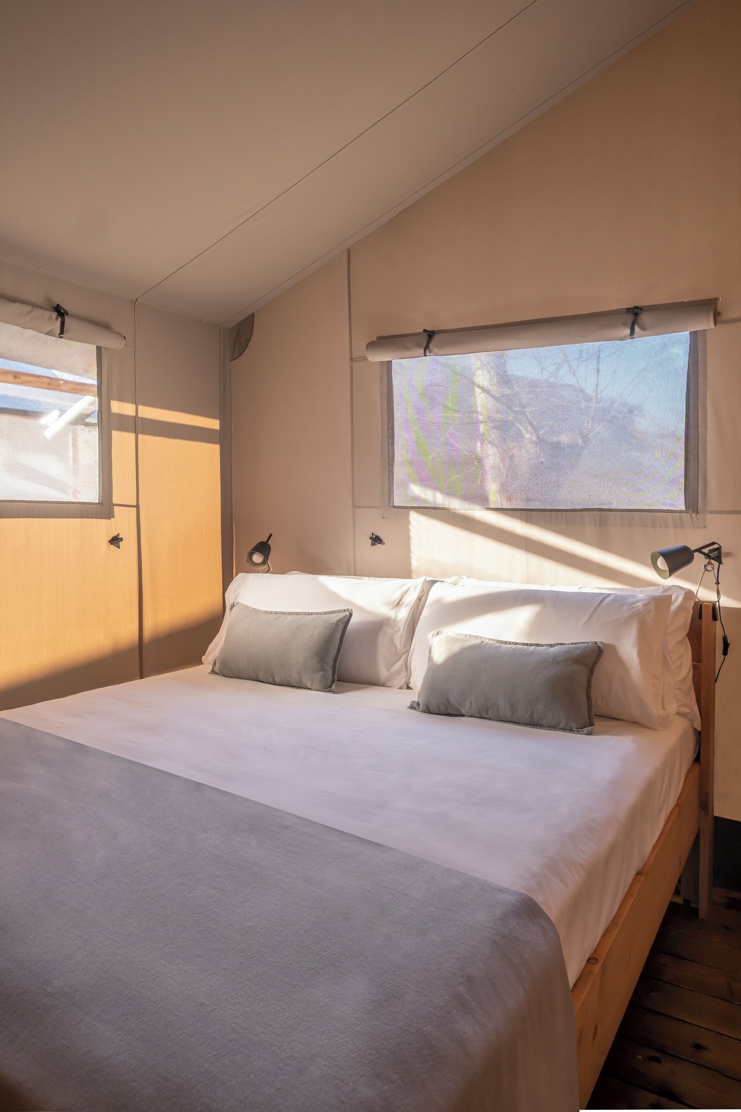 Quarto com cama grande, duas mesas de cabeceira, janela com persianas e vista para árvores.