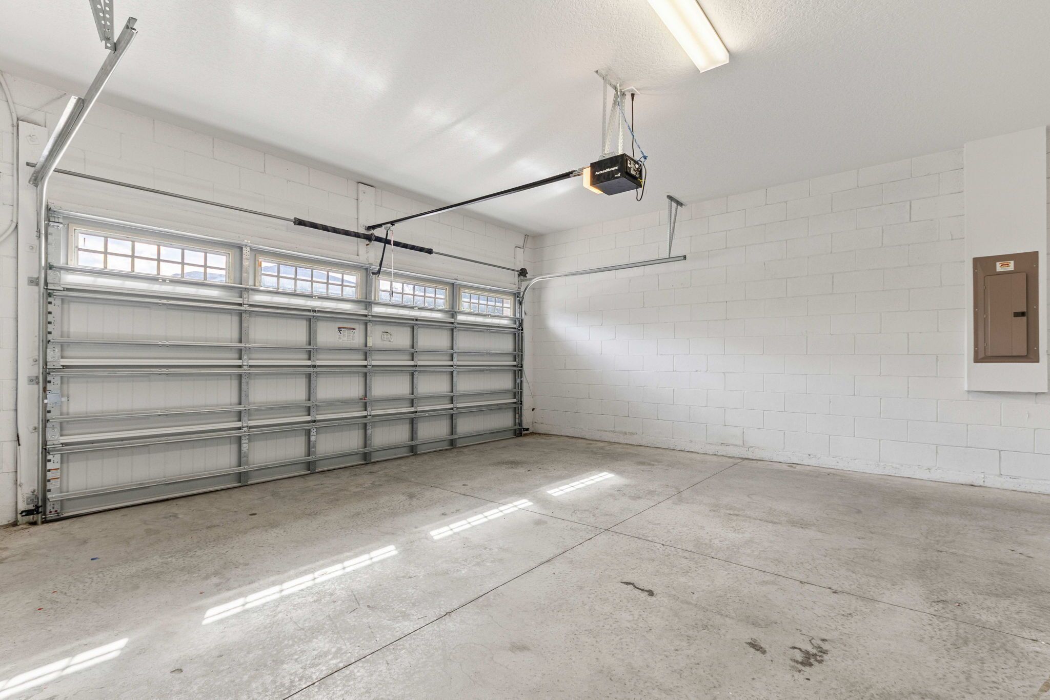 Uma garagem limpa e vazia, com uma grande porta de metal, paredes de tijolo branco e um projetor fixado no teto.