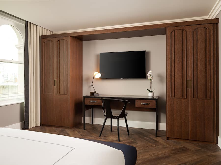 Quarto com cama, escrivaninha, cadeira, televisão e guarda-roupas de madeira.