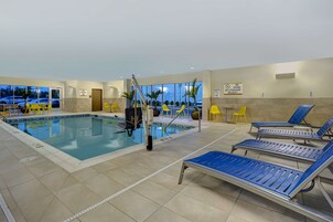 Piscina interna com espreguiçadeiras azuis, cadeiras amarelas e uma escadaria que leva a um andar superior.