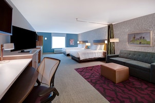Quarto de hotel com cama, sofá, escrivaninha com televisão e uma cadeira.