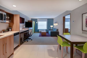 Quarto de hotel moderno com cozinha compacta, televisão de tela plana, sofá e área de refeições.