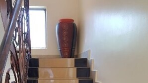 Uma escada com degraus alternados em bege e preto, um corrimão de madeira e um vaso vermelho no patamar.