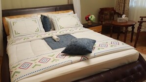 Cama bem arrumada com colcha estampada, almofadas e toalha enrolada.