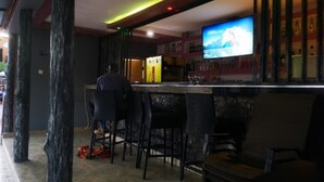 Uma área de bar com tela de televisão, banquetas e balcão.