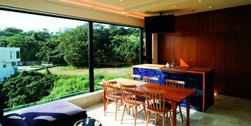 Cozinha moderna com mesa e cadeiras de madeira, painel de azulejos azuis e uma grande janela com vista para uma paisagem verde.