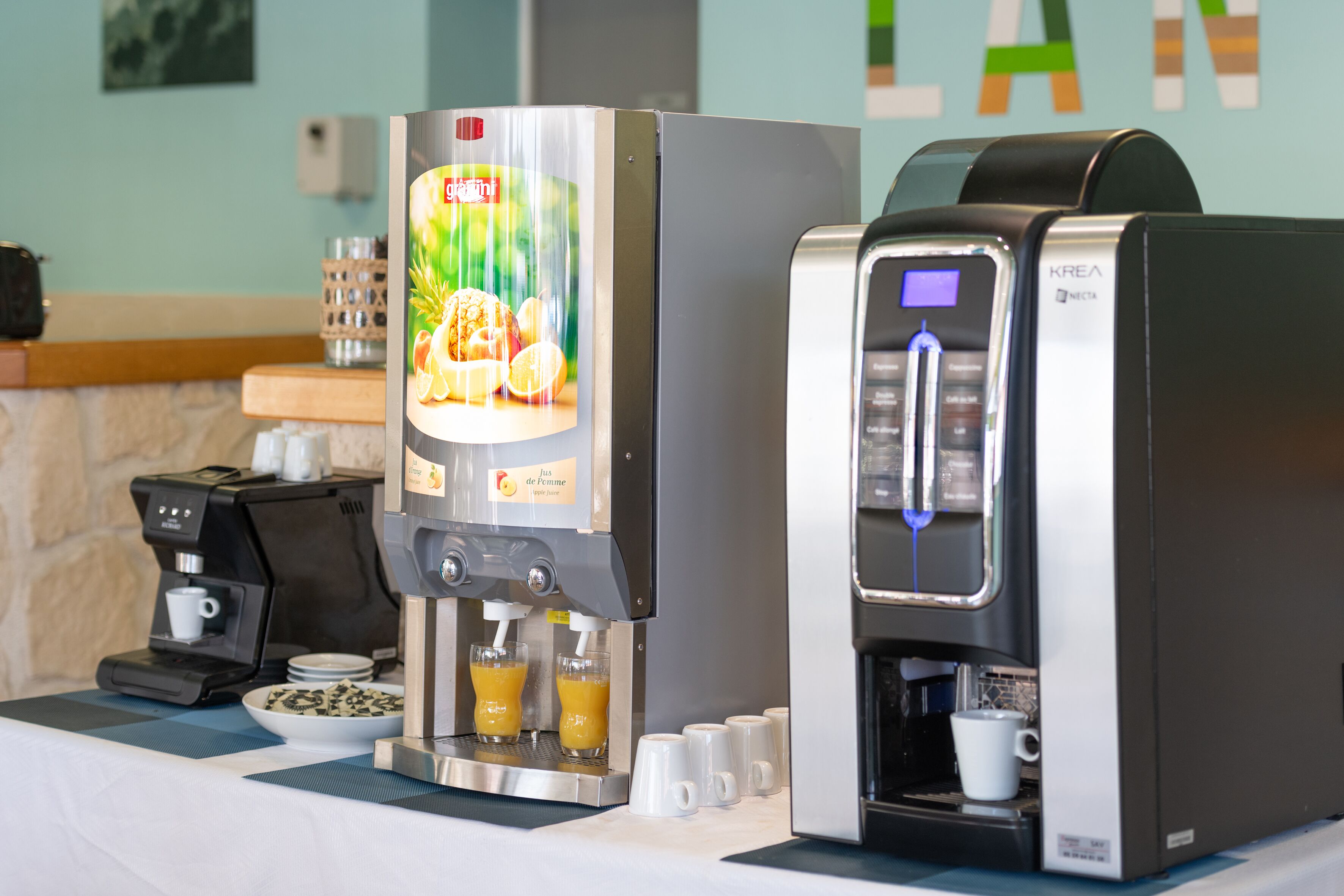 Uma estação de café com duas máquinas de espresso e um dispensador de bebidas.