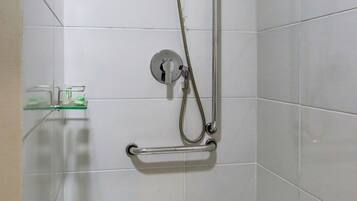 Um chuveiro com chuveiro manual, torneira fixa na parede e prateleira de vidro com artigos de higiene pessoal.