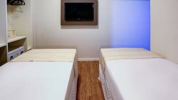 Quarto com duas camas, televisão na parede e piso de madeira.