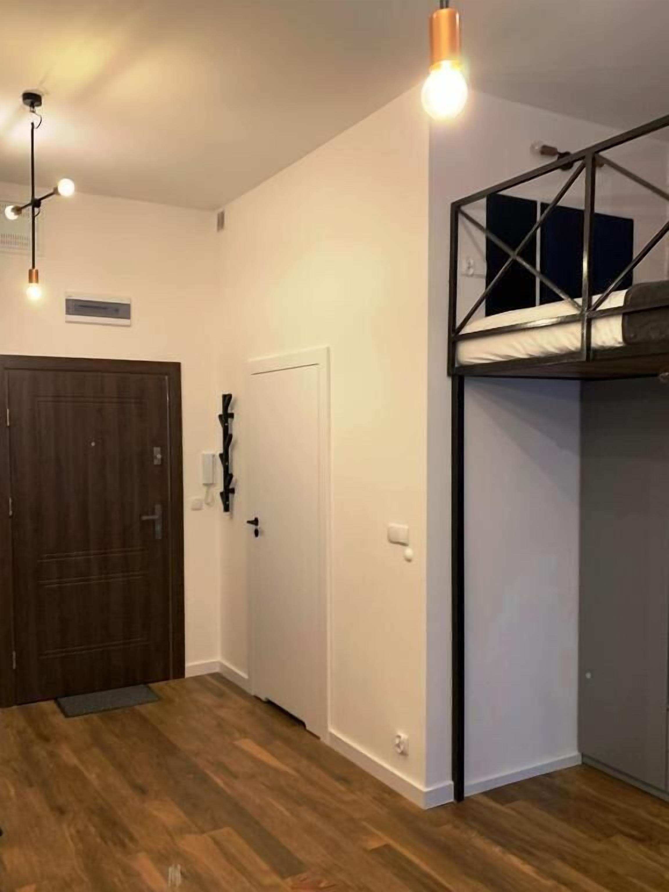 Quarto com beliche, porta de madeira, parede branca e luminária no teto.