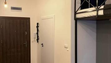 Quarto com beliche, porta de madeira, parede branca e luminária no teto.
