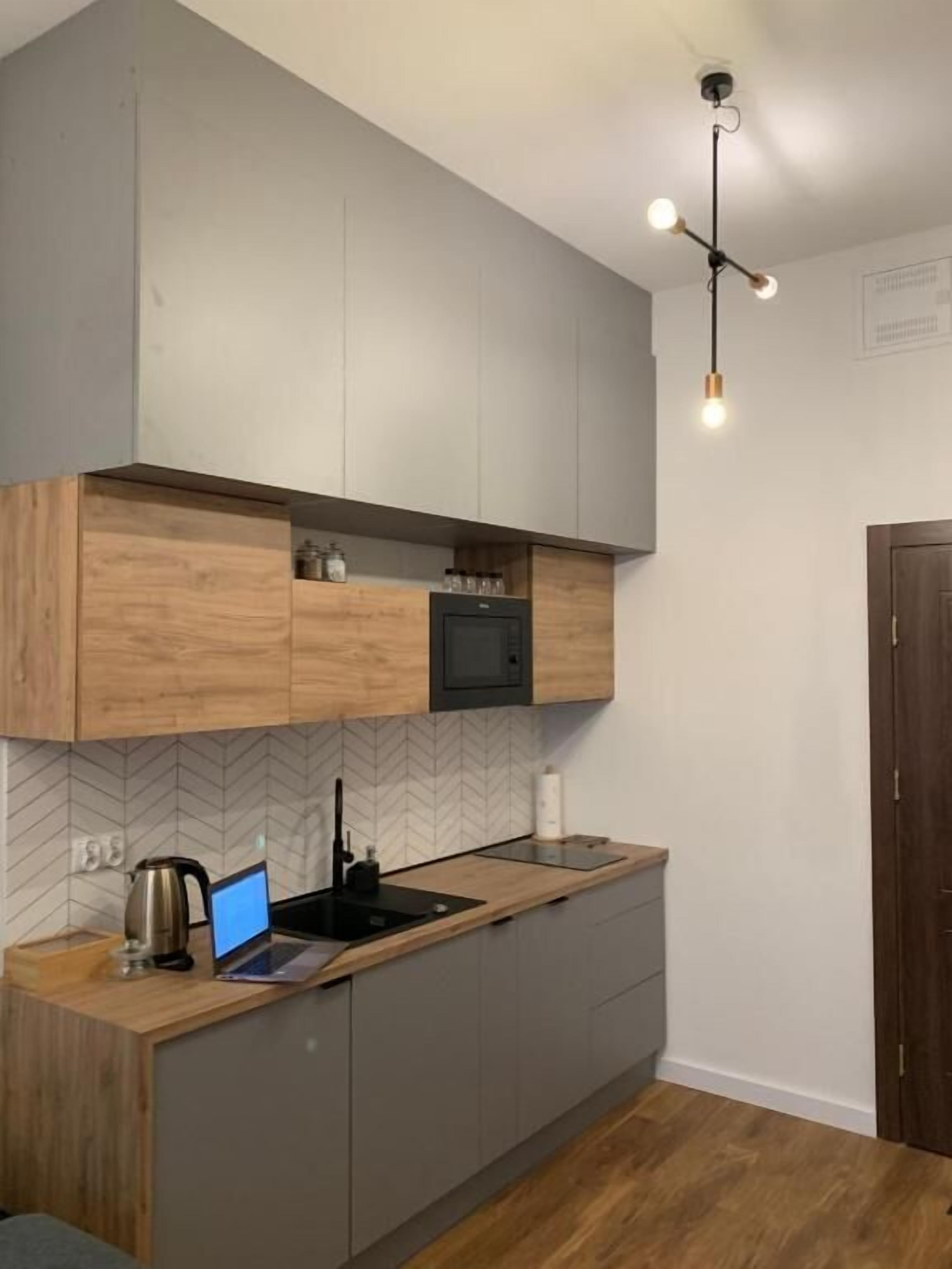 Cozinha moderna com armários cinza, bancadas de madeira, micro-ondas embutido e um laptop no balcão.