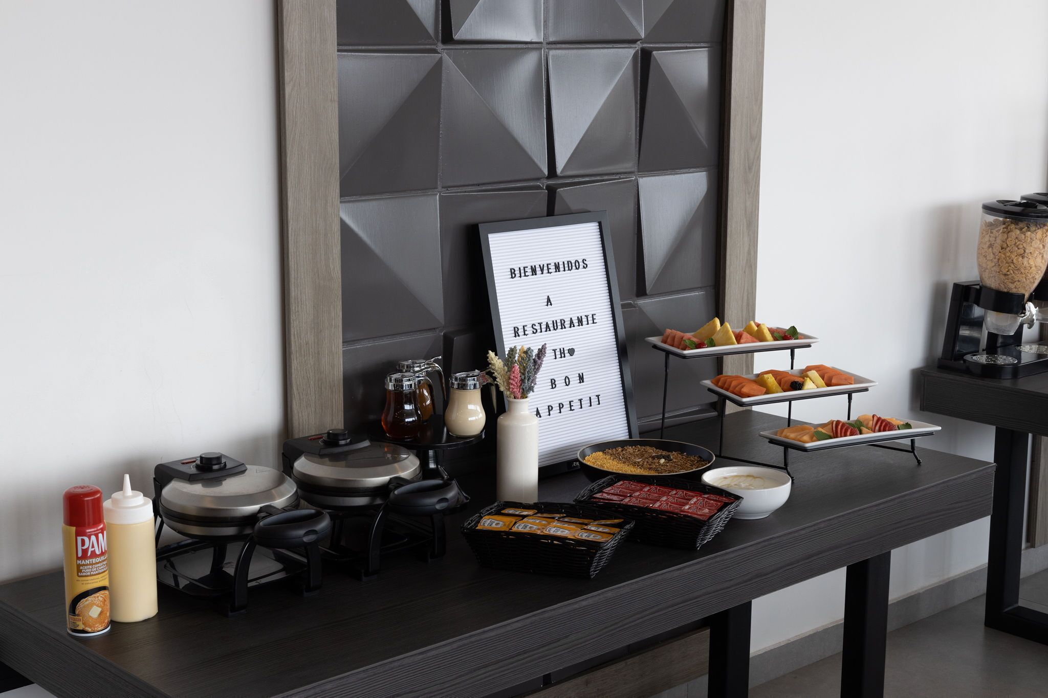 Disposição de buffet com placa de boas-vindas, diversos alimentos, acompanhamentos e uma máquina de café.