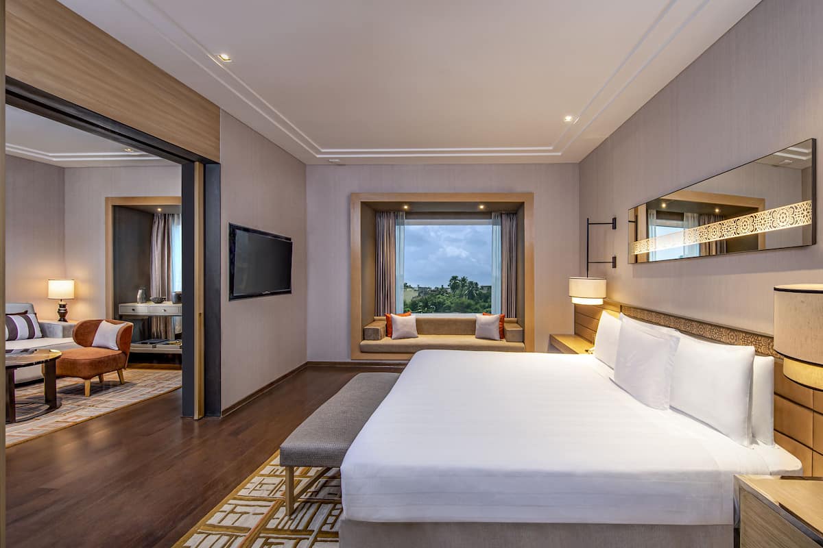 Quarto de hotel com uma cama grande, um sofá, uma TV e uma janela com vista.