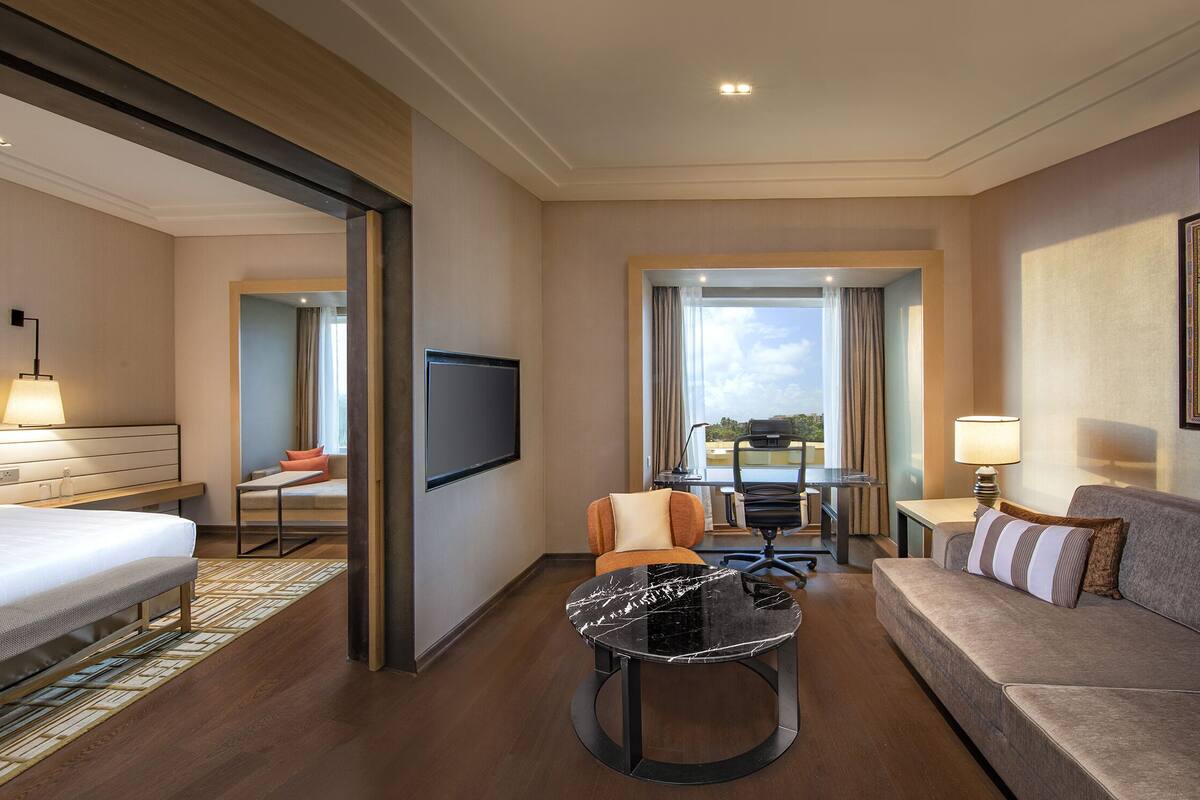 Quarto de hotel com cama, sofá, escrivaninha, cadeira e televisão.