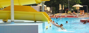 Uma área de piscina com um escorrega aquático amarelo e vários guarda-sóis.