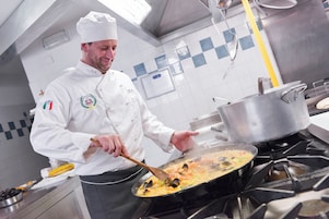 Um chef em uma cozinha profissional com eletrodomésticos de aço inoxidável e ladrilhos quadriculados.
