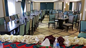 Uma sala de conferências de hotel com várias mesas e cadeiras, garrafas de água sobre as mesas e uma pilha de roupas amassadas no chão.