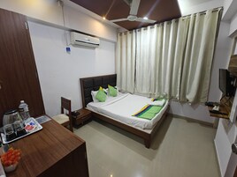 Quarto de hotel com uma cama, uma escrivaninha com uma garrafa de água, um controle remoto e uma televisão.