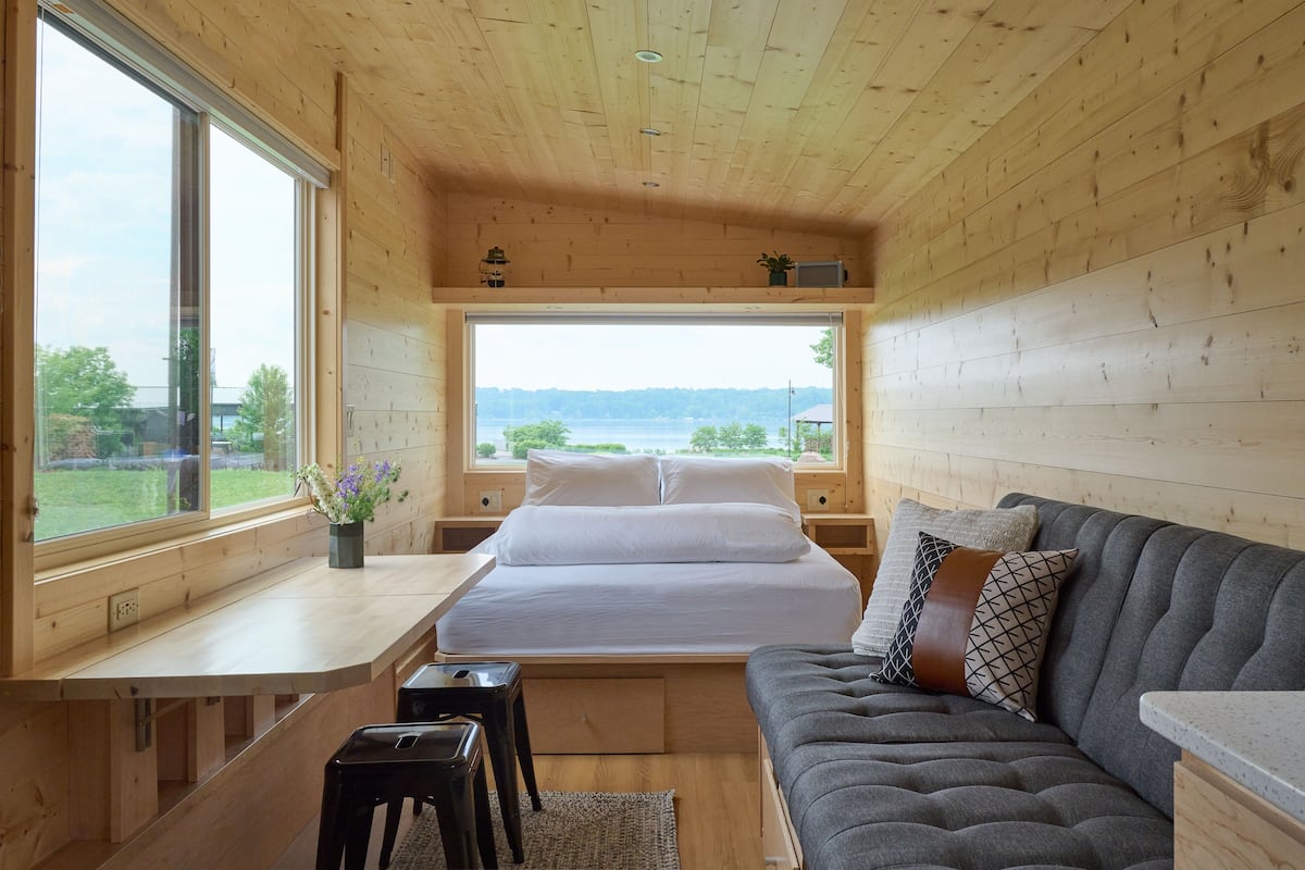 Quarto com cama, sofá, escrivaninha e janela com vista para o exterior.