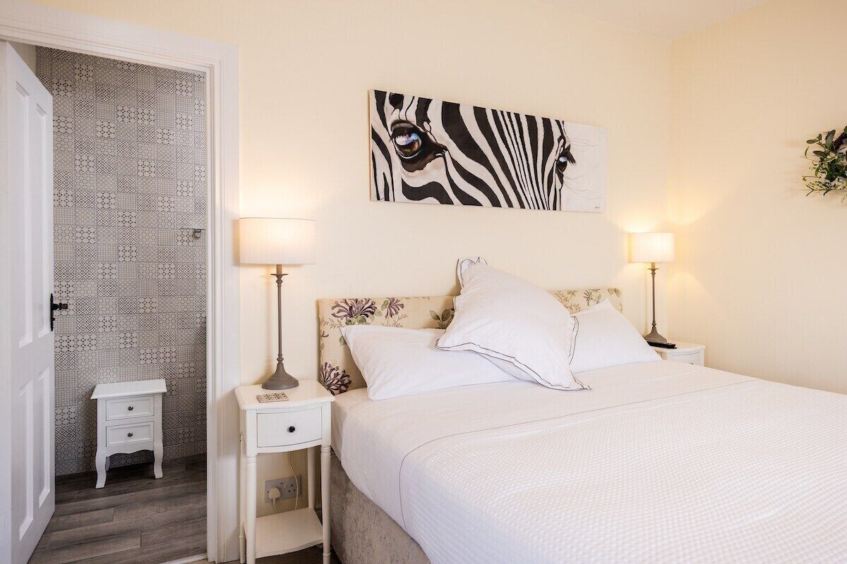 Quarto com uma cama, duas mesas de cabeceira com luminárias, uma obra de arte de zebra na parede e papel de parede estampado na parede esquerda.