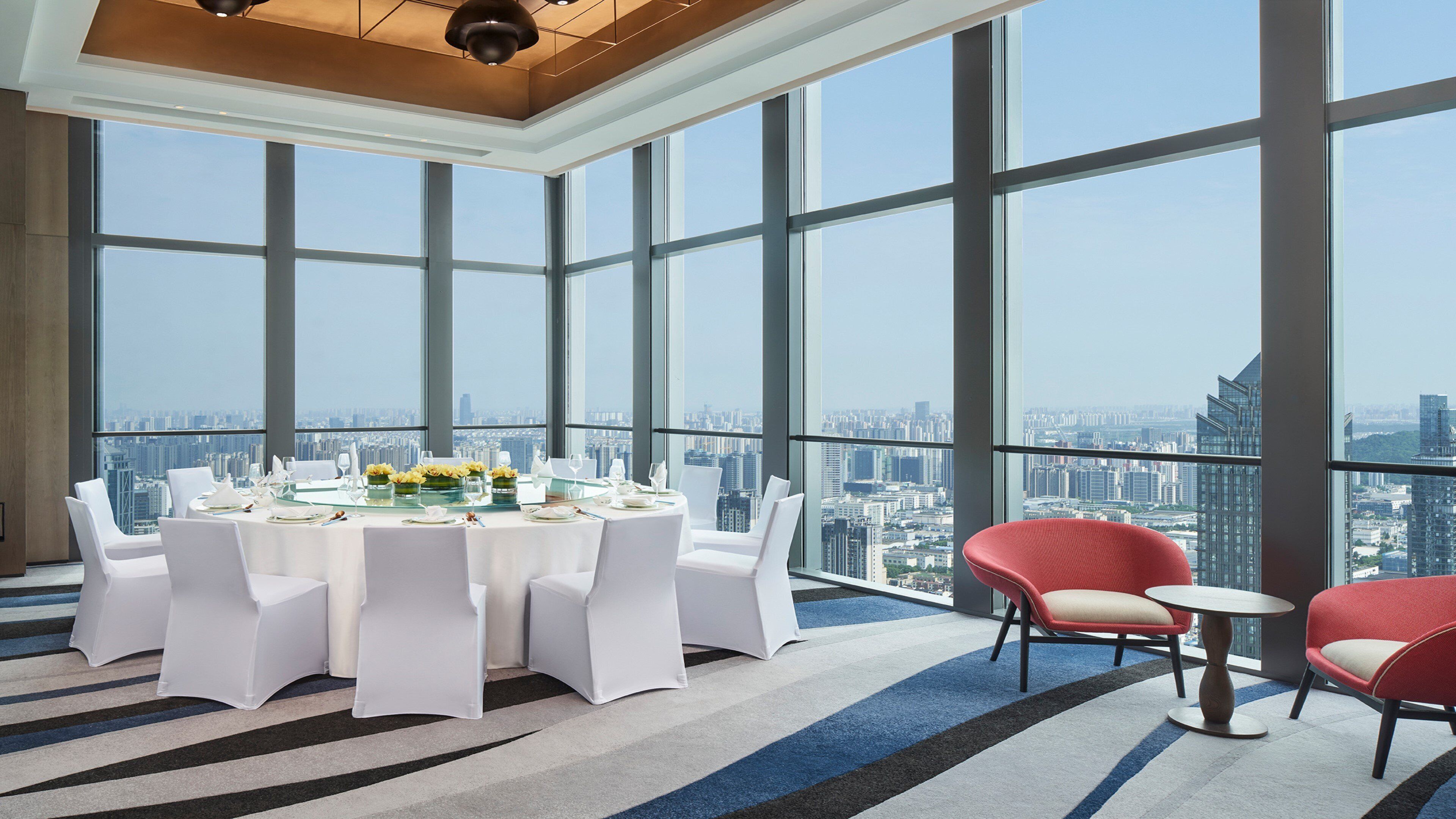 Uma área de refeições em um edifício alto com vista panorâmica da cidade, grandes janelas e design de interiores moderno.