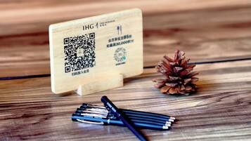 Um cartão de madeira com código QR e texto, um pinhão e canetas sobre uma superfície de madeira.