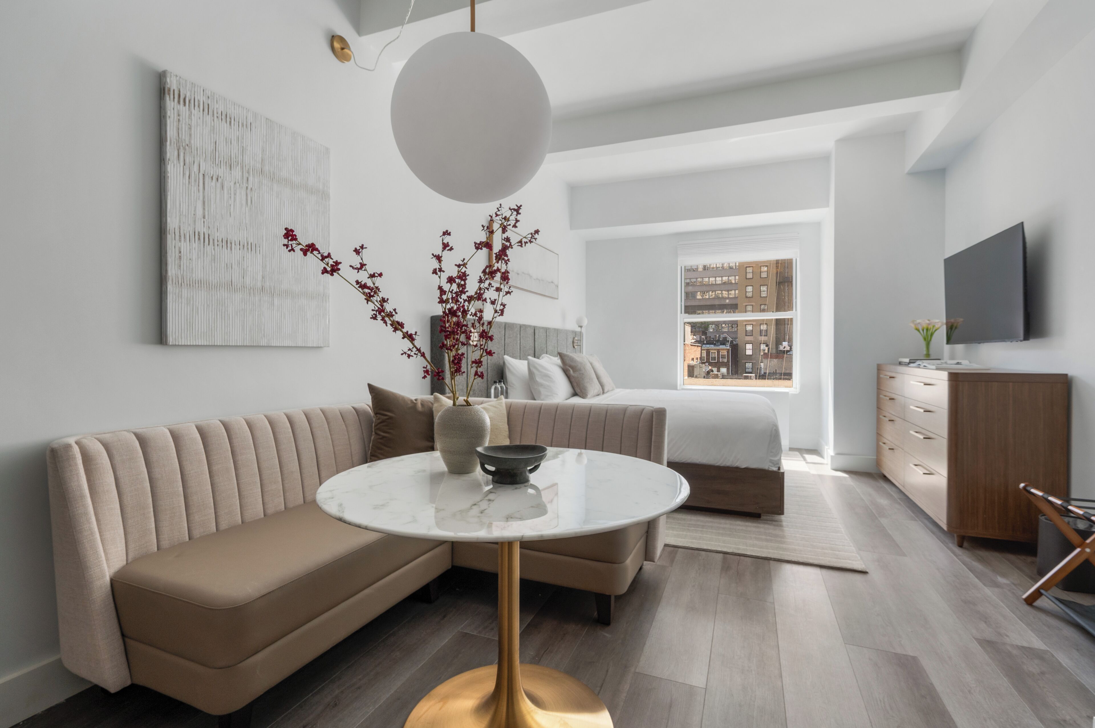 Quarto moderno com cama, sofá, televisão e janela com vista para a cidade.