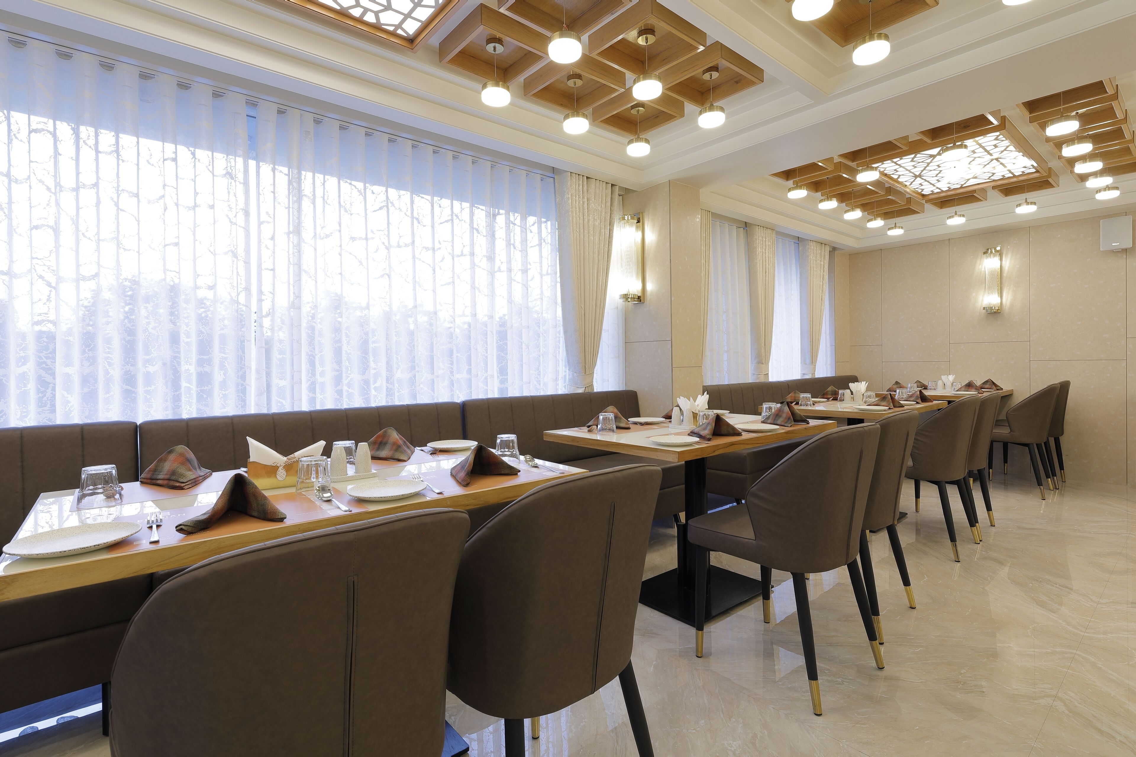 Uma sala de jantar com mesas compridas, cadeiras marrons e um design de teto moderno.