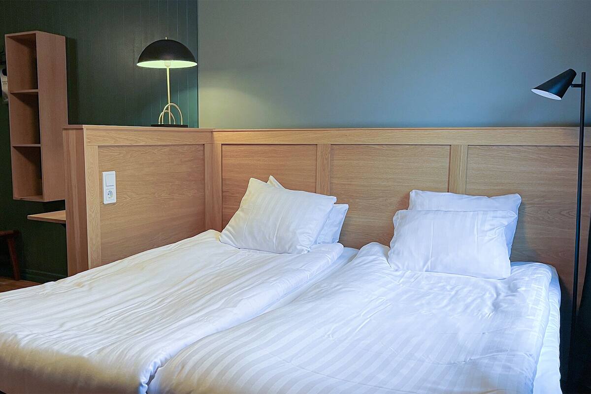 Uma cama bem arrumada com lençóis brancos, cabeceira de madeira e luminária de cabeceira.