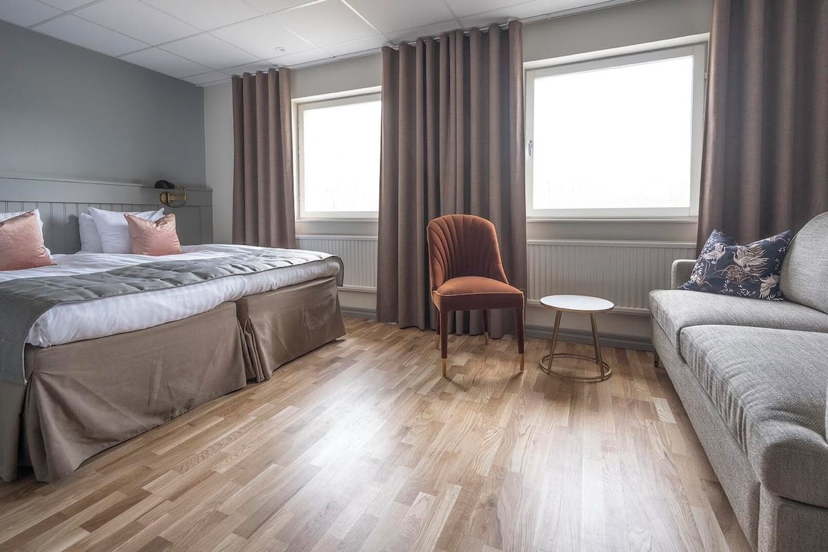 Quarto de hotel com cama, poltrona, mesa pequena e sofá.
