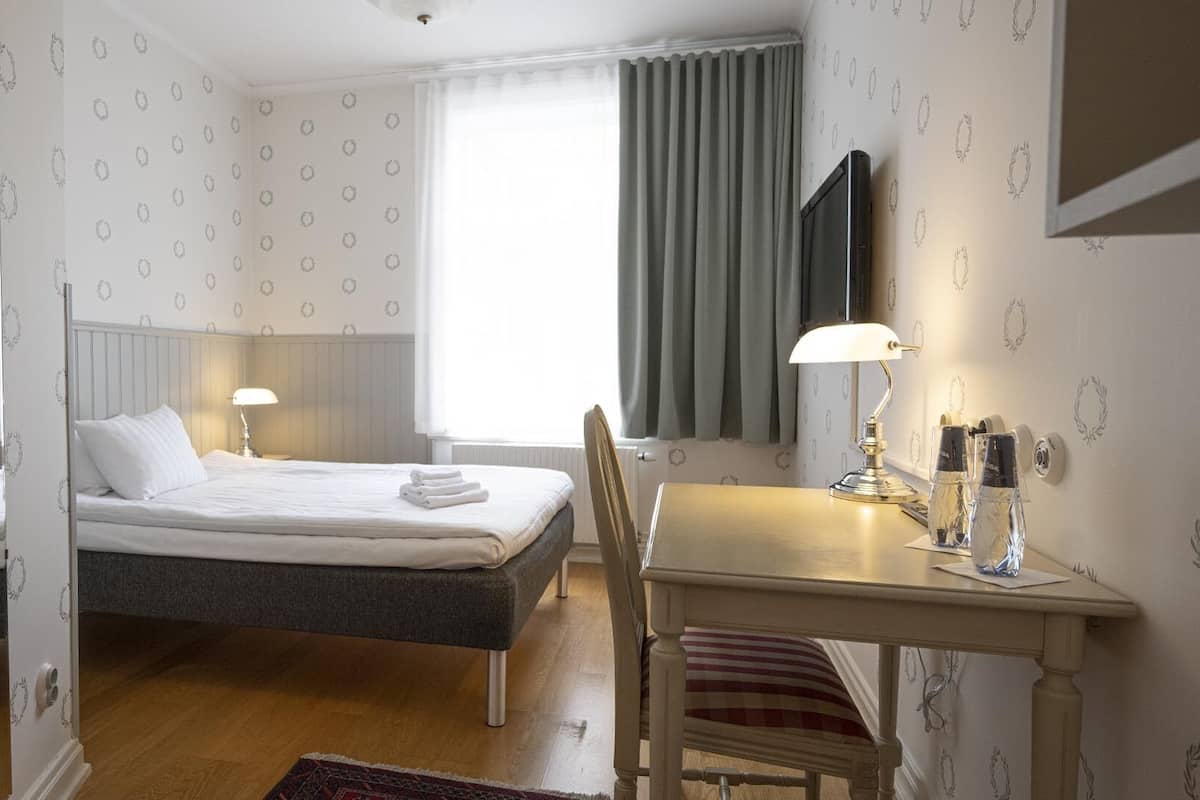 Quarto de hotel com cama, escrivaninha, cadeira, televisão e janela com cortinas.