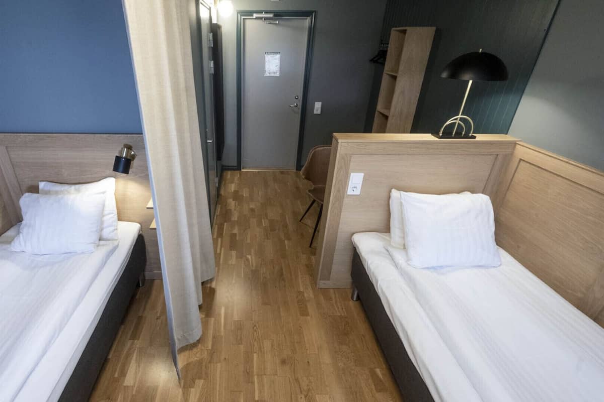 Quarto de hotel com duas camas de solteiro, piso de madeira, escrivaninha e uma cadeira.
